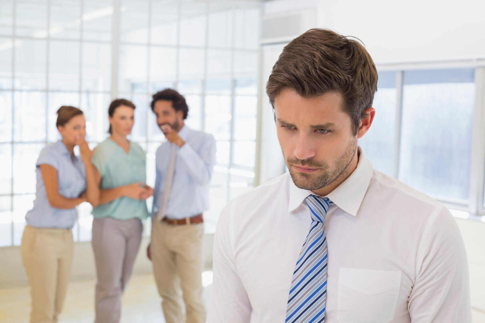 Office workers gossiping behind a worker who looks downcast